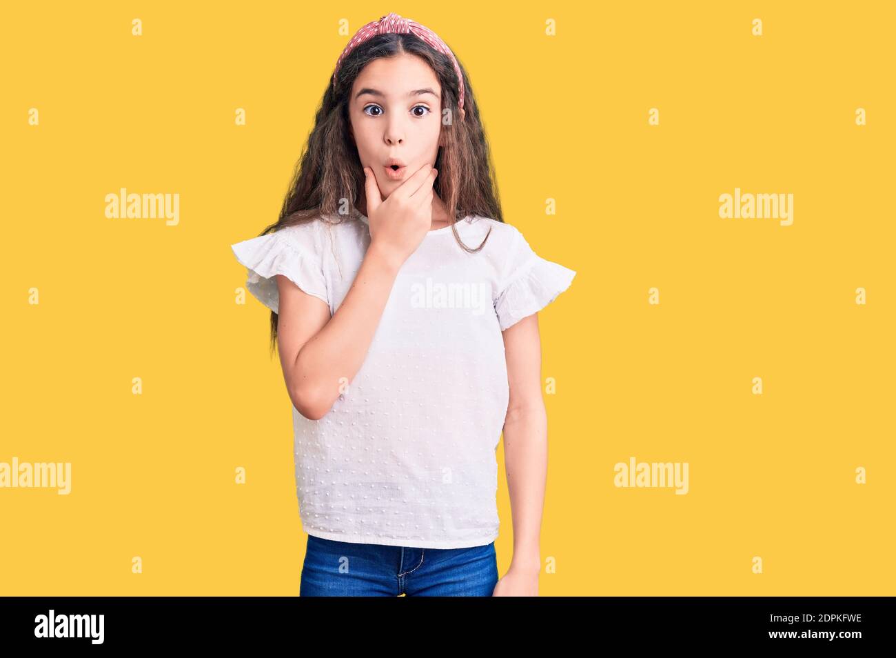 Cute hispanic child girl wearing casual white tshirt looking fascinated ...