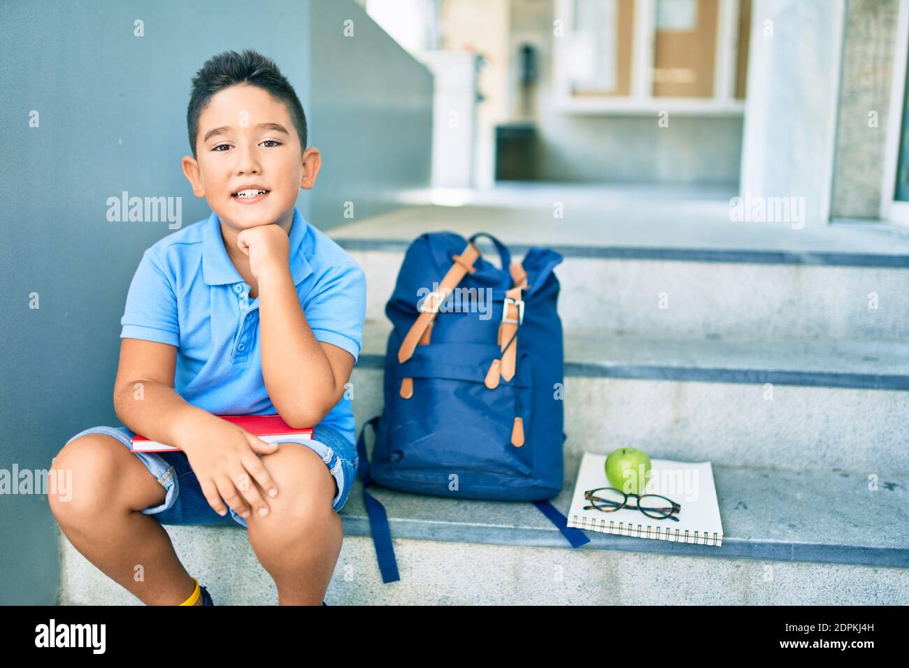 Adorable student boy smiling happy sitting on the stairs at school ...