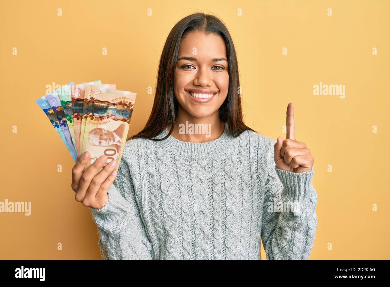 Beautiful hispanic woman holding canadian dollars smiling with an idea ...