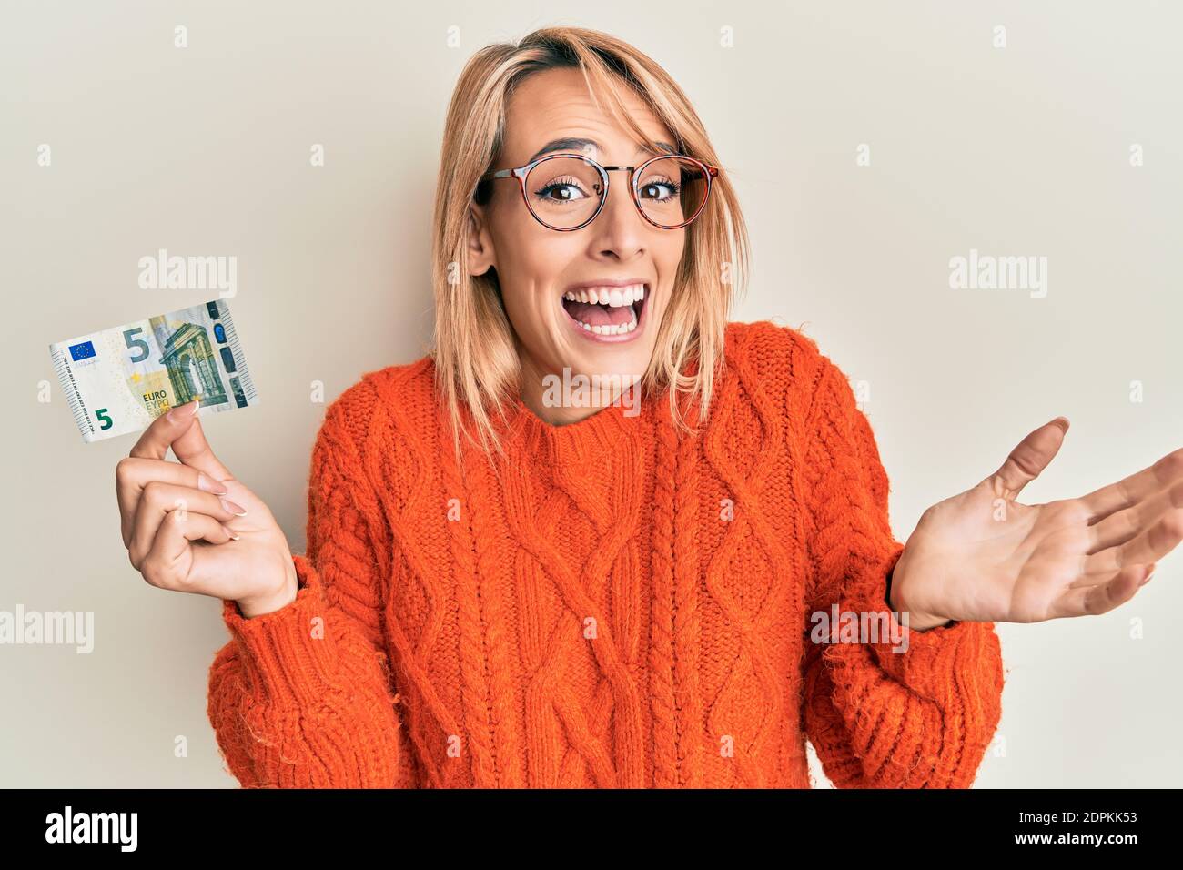 Beautiful blonde woman holding 5 euro banknote celebrating achievement ...