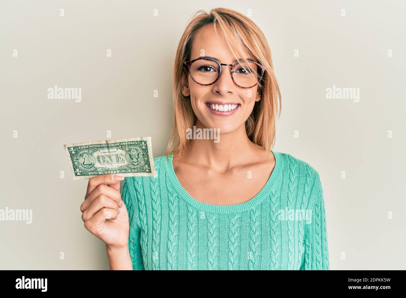 Beautiful blonde woman holding 1 dollar banknote looking positive and ...