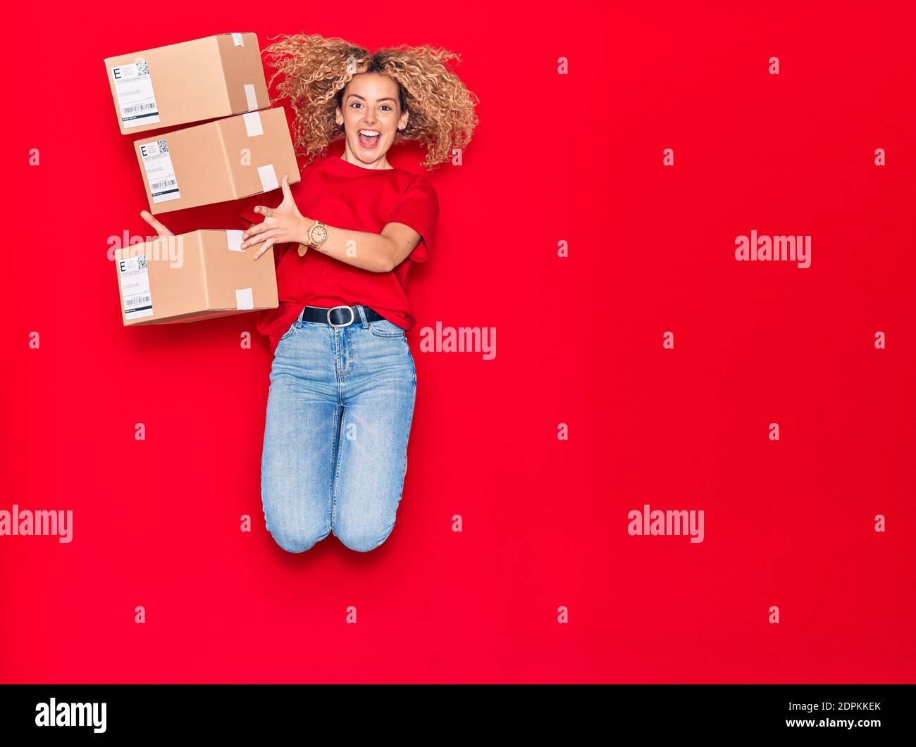 Young beautiful curly deliverywoman holding package smiling happy ...