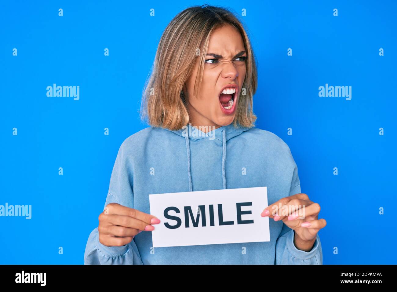 Beautiful caucasian woman holding smile text angry and mad screaming ...