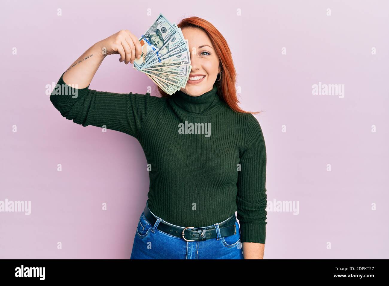 Beautiful redhead woman holding dollars banknote over eye looking ...