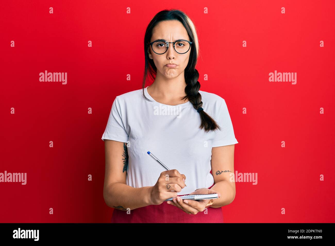 Young hispanic woman wearing waitress apron taking order depressed and ...