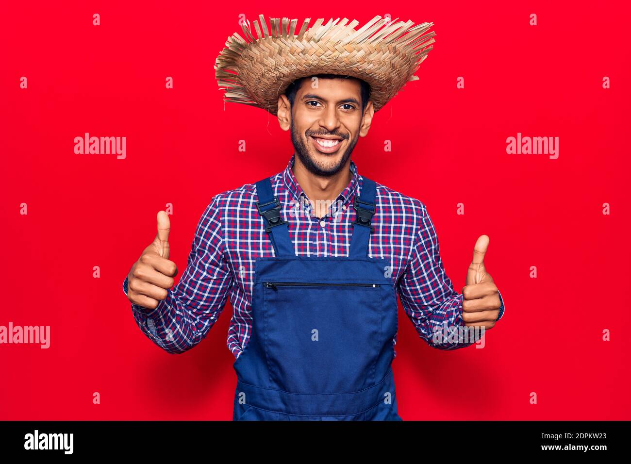 Young latin man wearing farmer hat and apron success sign doing ...