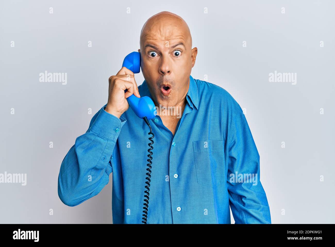 Middle age bald man speaking on vintage telephone scared and amazed ...