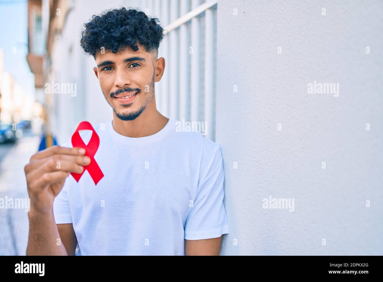 Young arab man smiling happy holding hiv awaraness red ribbon leaning ...