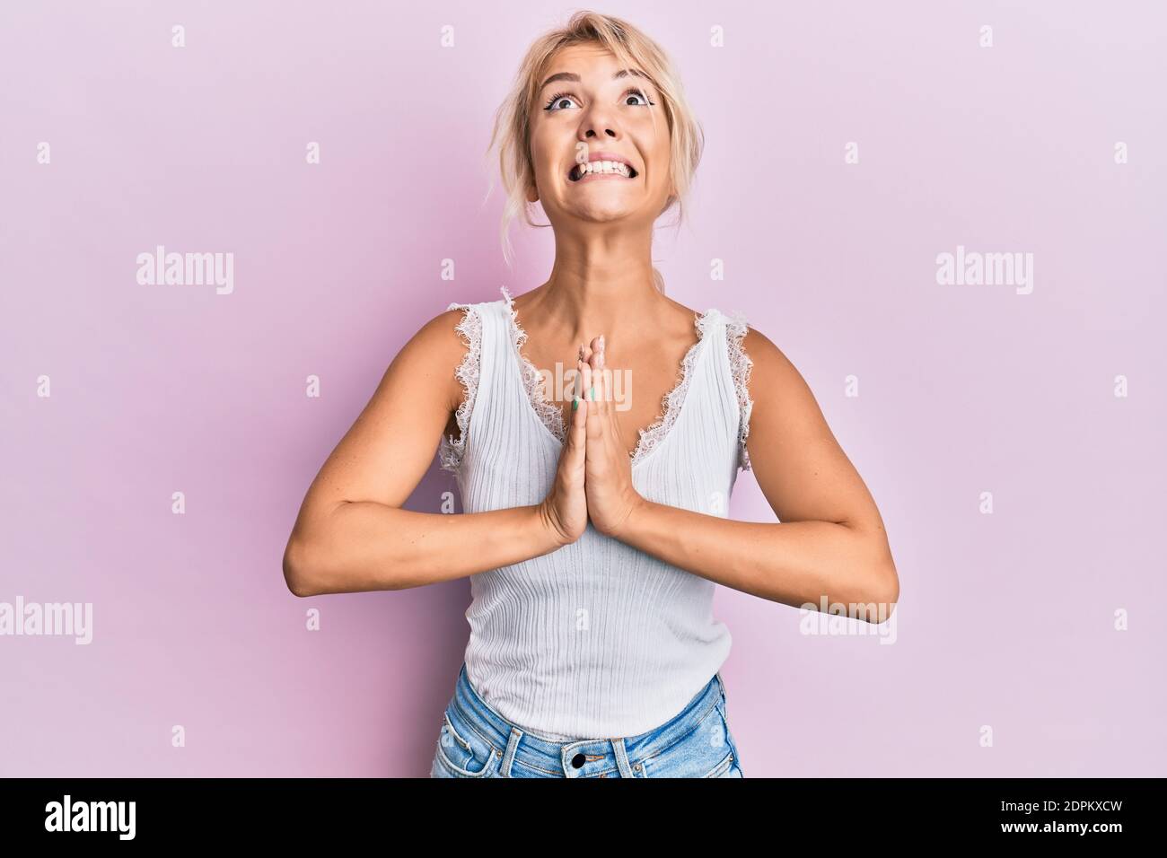 Young blonde girl wearing casual clothes begging and praying with hands ...