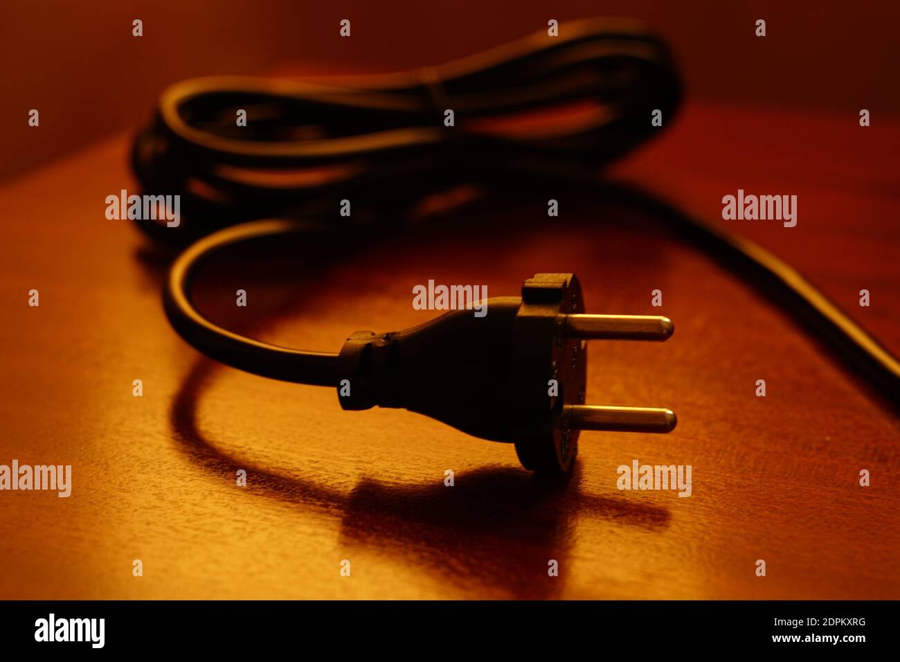 Black plug with a skein of wire on a brown wooden table with shadow ...
