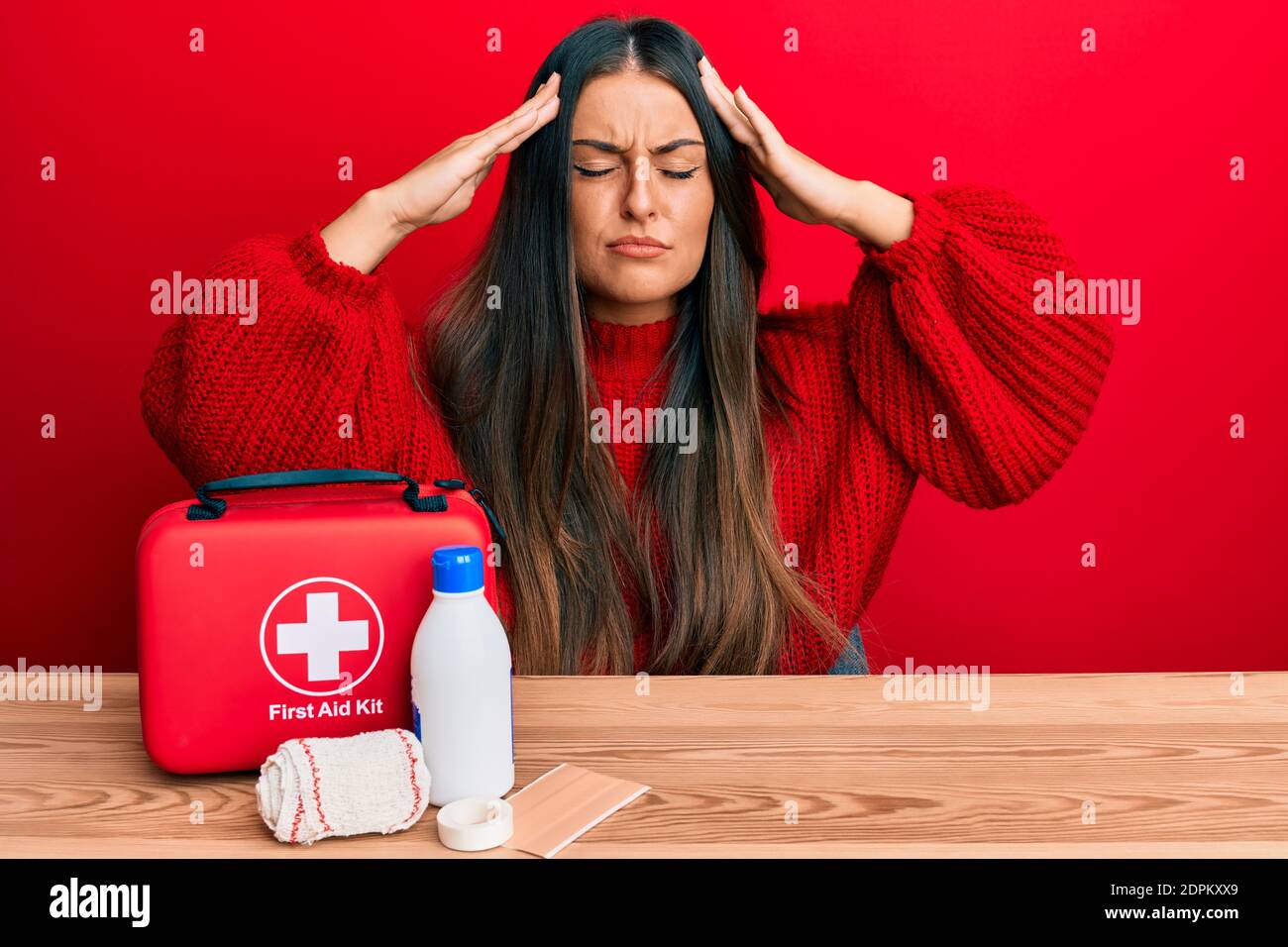 Beautiful hispanic woman with first aid kit with hand on head, headache ...
