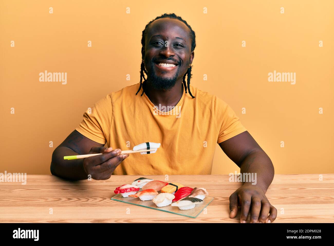 Handsome young black man eating sushi sitting on the table looking ...