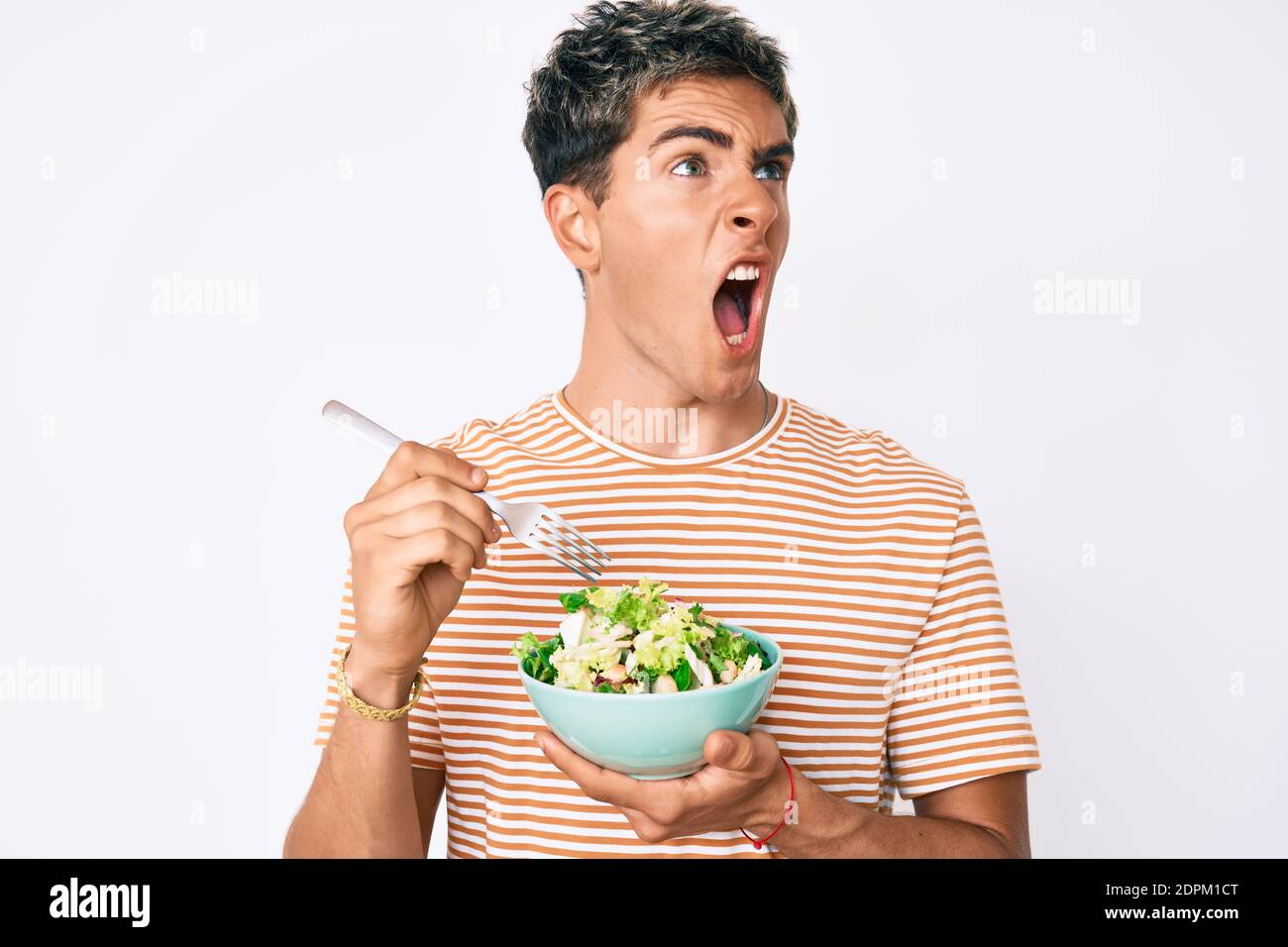 Young handsome man eating salad angry and mad screaming frustrated and ...
