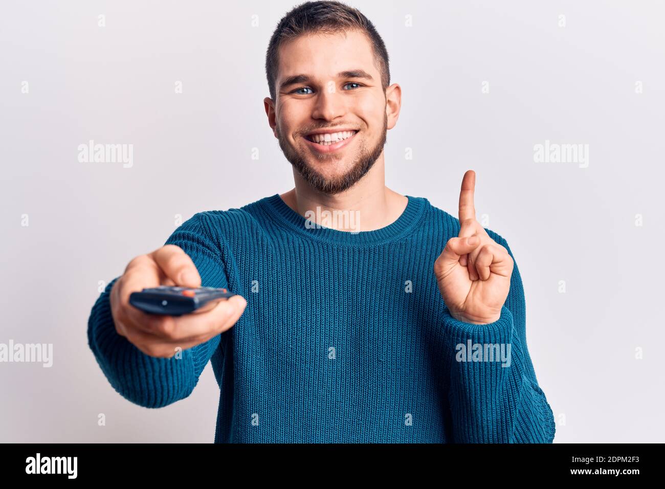 Young handsome man holding tv remote control smiling with an idea or ...