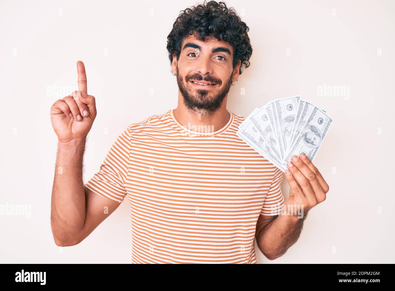 Handsome young man with curly hair and bear holding money bag with ...