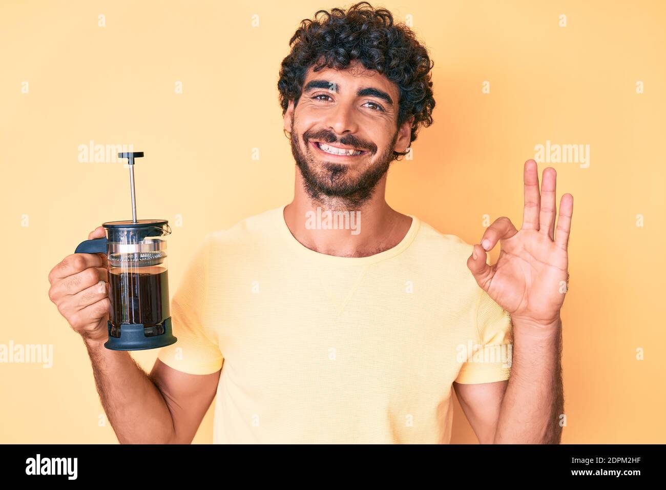 Handsome young man with curly hair and bear holding french coffee maker ...