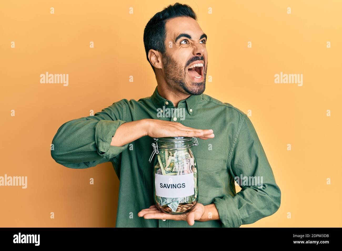 Young hispanic man holding jar with savings angry and mad screaming ...