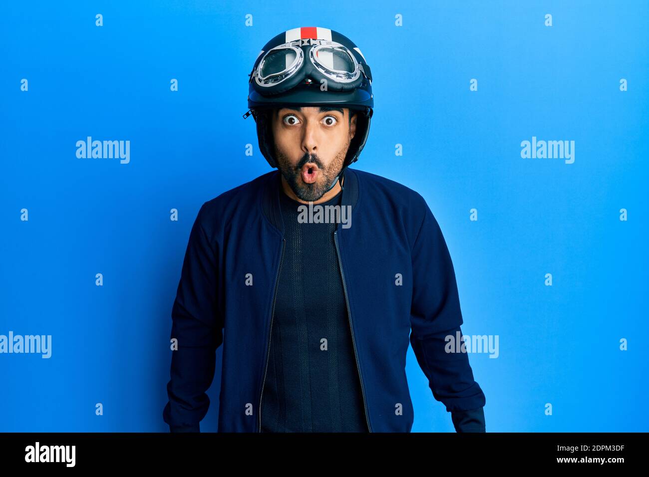 Young hispanic man holding motorcycle helmet scared and amazed with ...