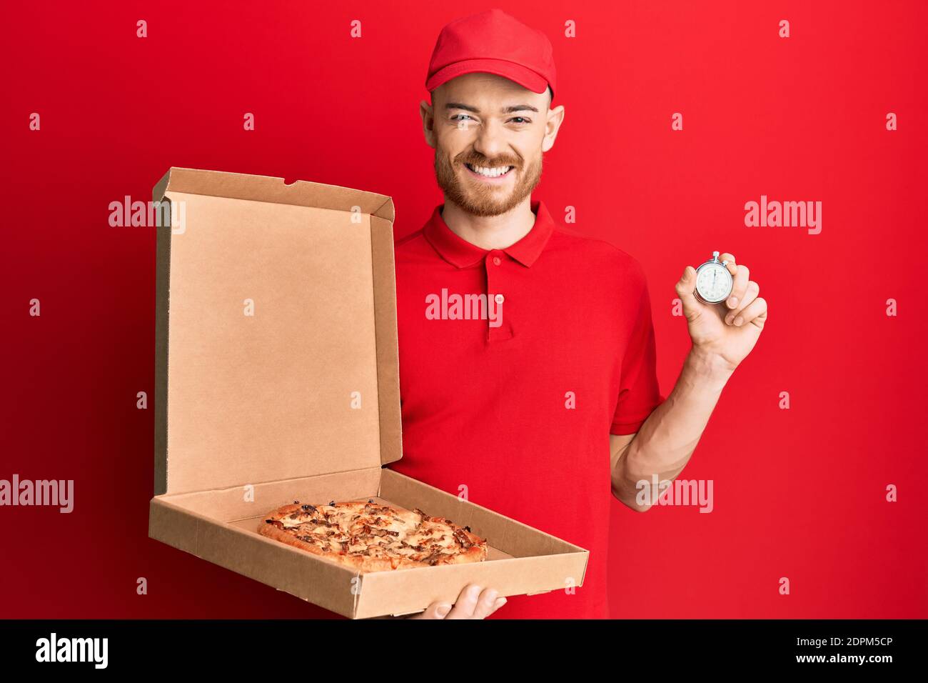 Young redhead man wearing delivery uniform holding pizza box and ...