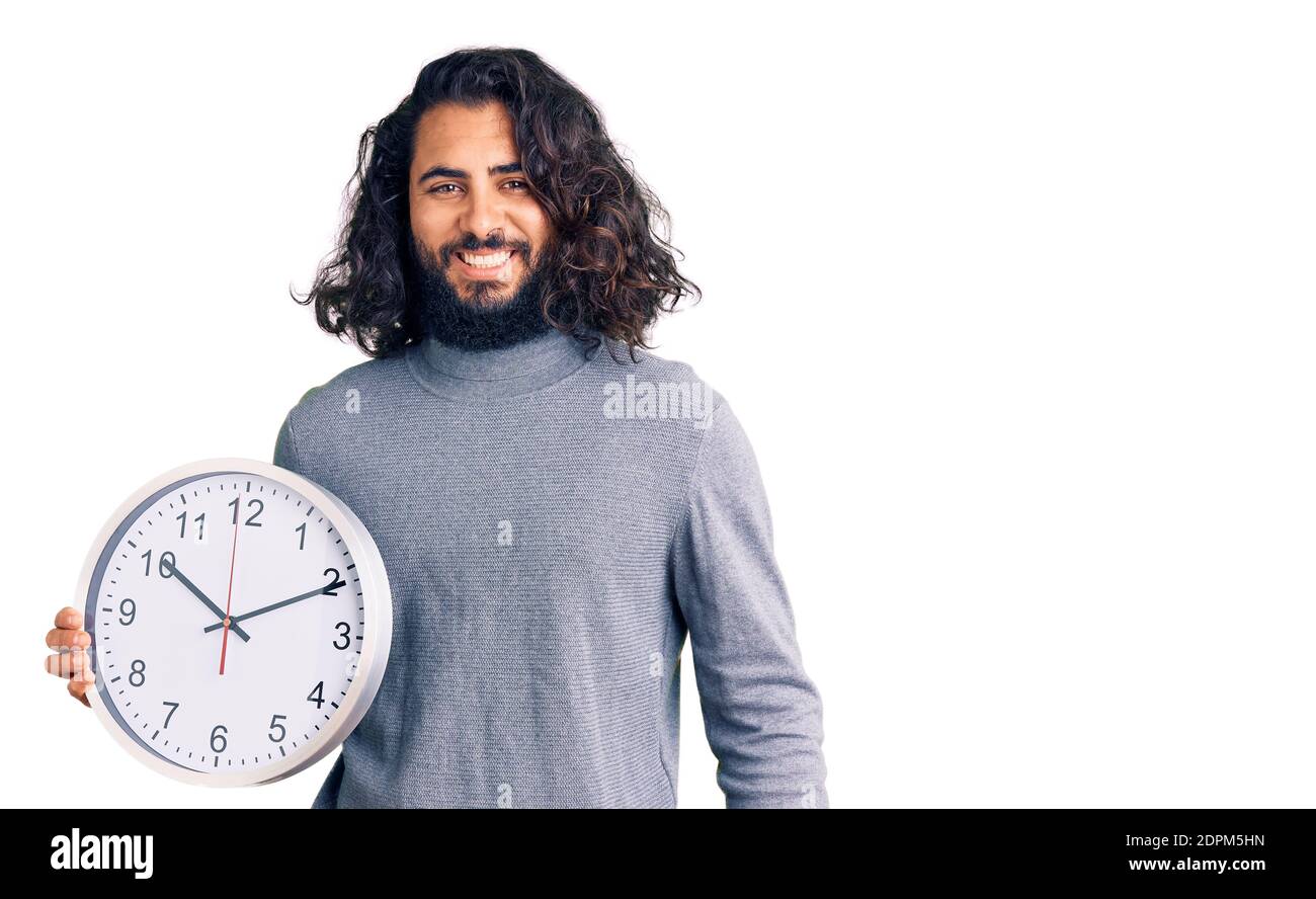 Young arab man holding big clock looking positive and happy standing ...