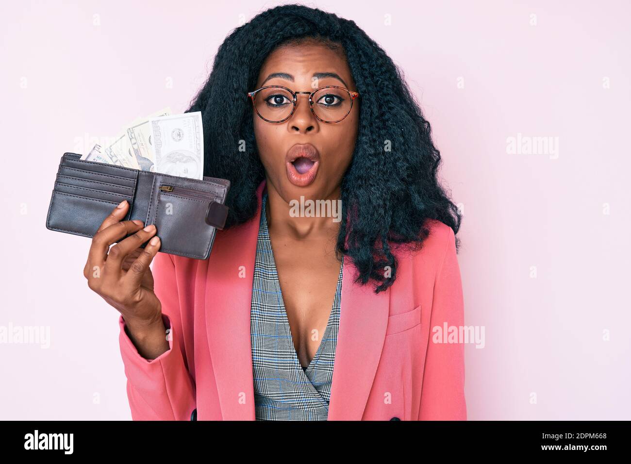Beautiful african woman holding wallet with dollars scared and amazed ...