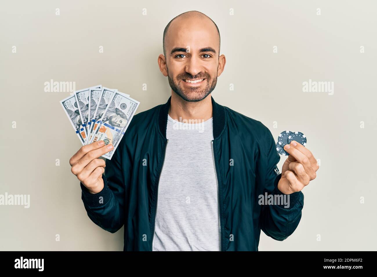 Young hispanic man playing poker holding dollars banknotes and chips ...