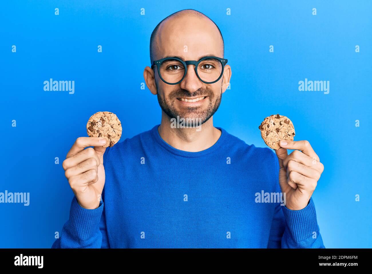 Young hispanic man holding chocolate chips cookies smiling with a happy ...