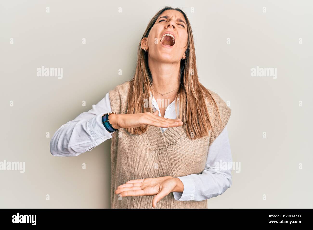 Brunette young woman doing size gesture holding invisible object angry ...