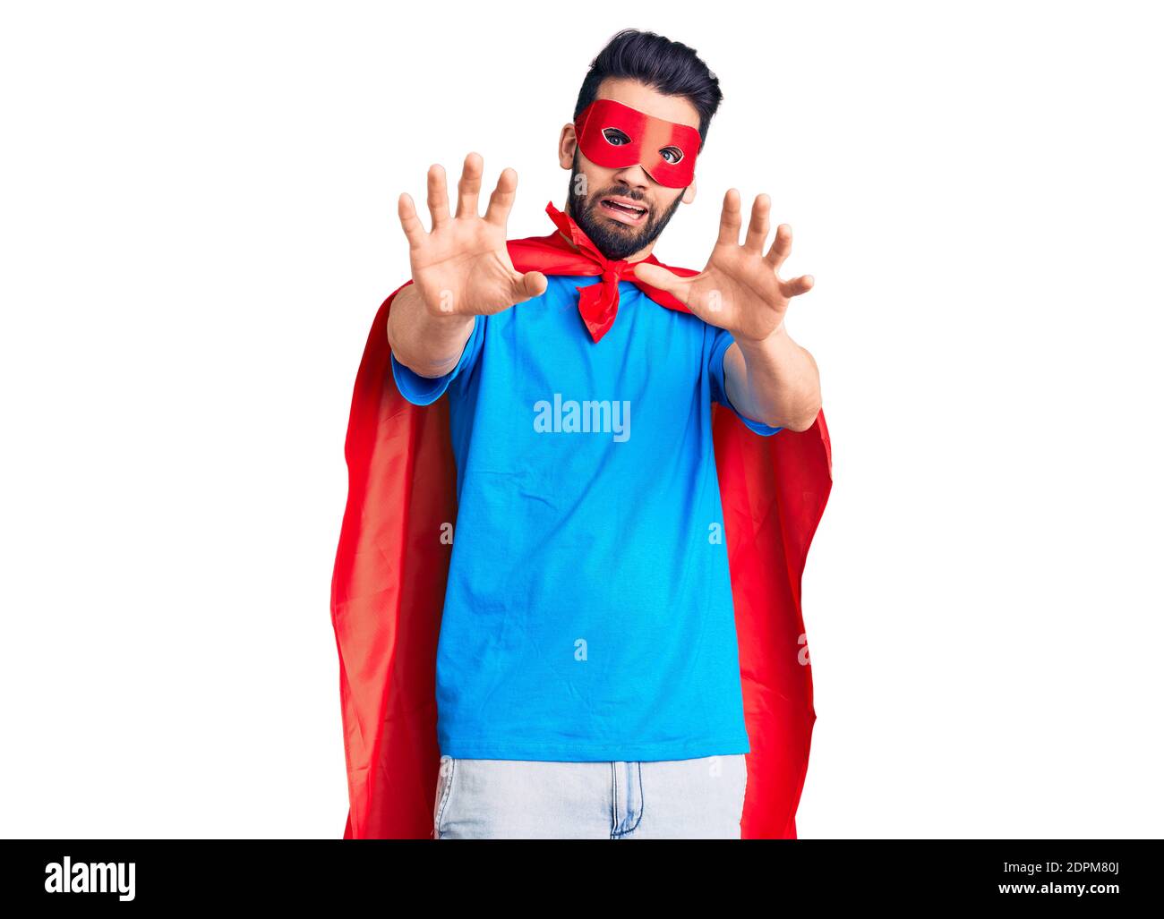Young handsome man with beard wearing super hero costume afraid and ...