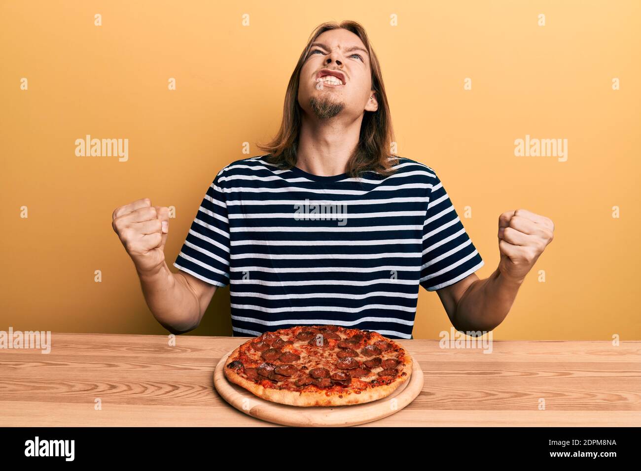 Handsome caucasian man with long hair eating tasty pepperoni pizza ...