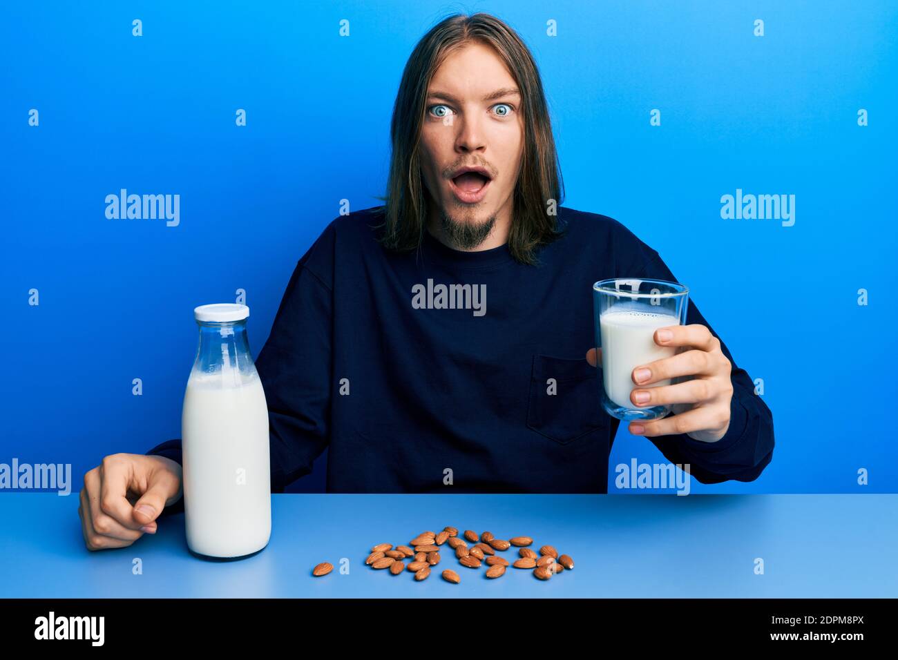 Handsome caucasian man with long hair drinking healthy almond milk ...