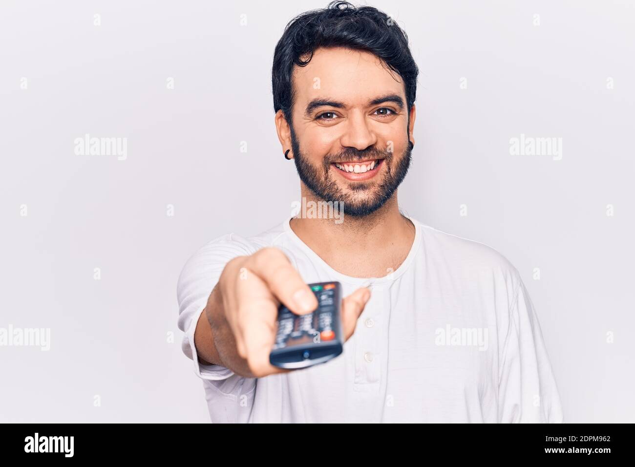Young hispanic man holding television remote control looking positive ...
