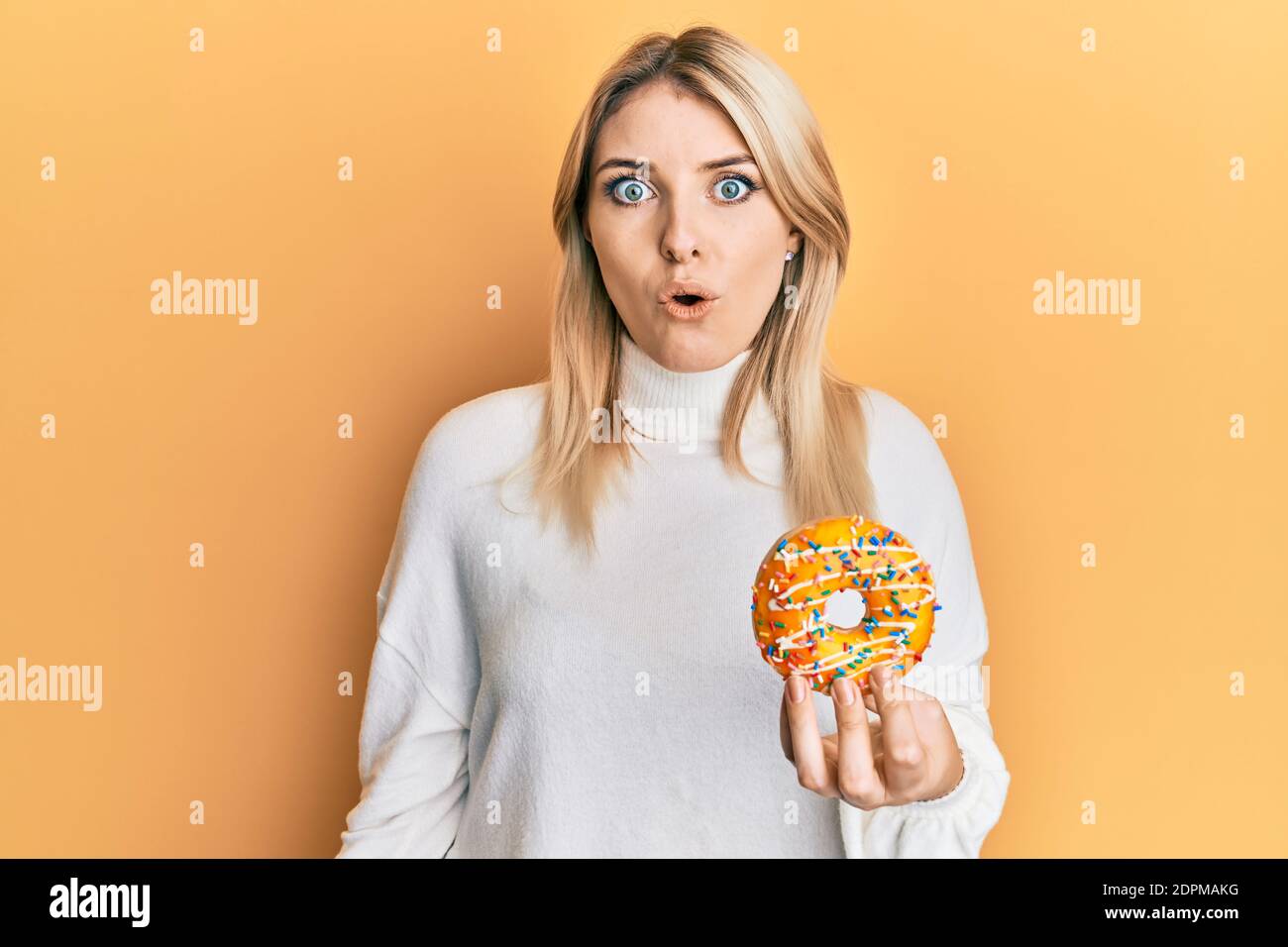 Young caucasian woman holding donut scared and amazed with open mouth ...