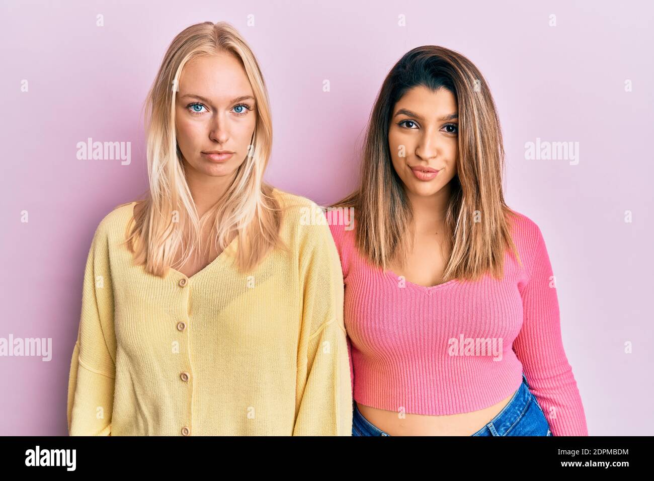 Two friends standing together over pink background relaxed with serious ...