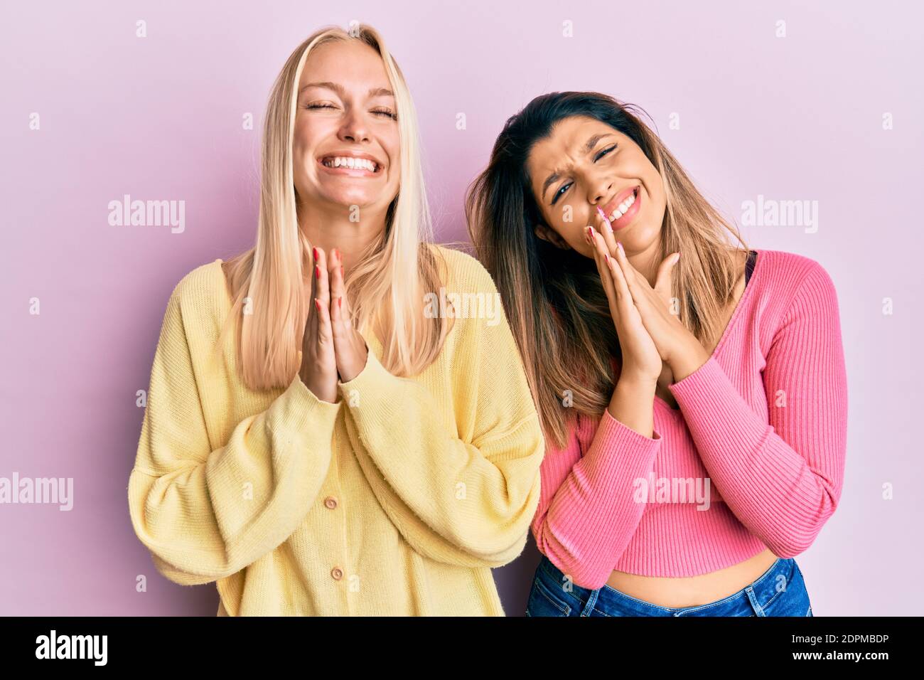 Two friends standing together over pink background begging and praying ...