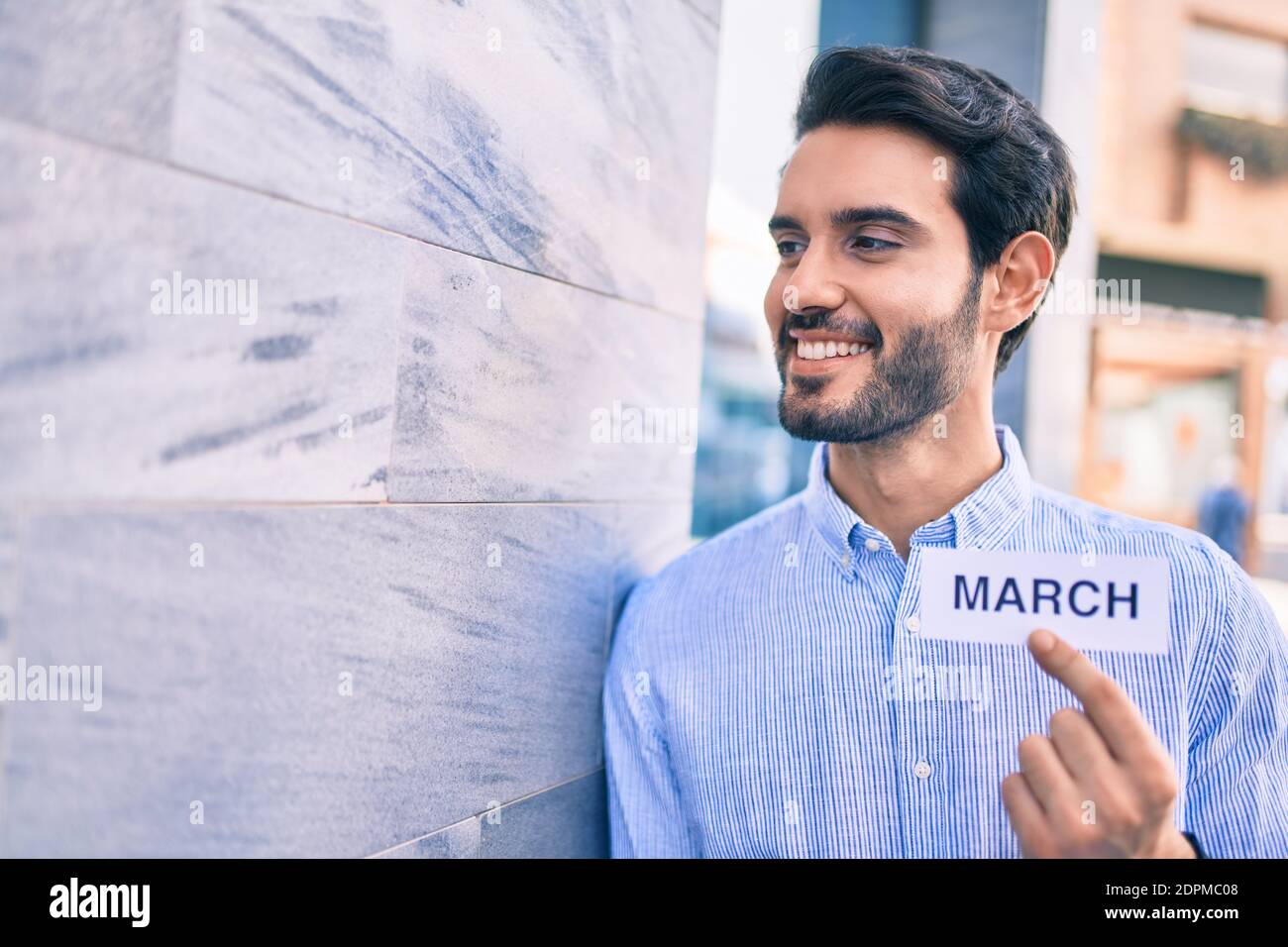 Young hispanic man smiling happy holding march word on paper leaning on ...