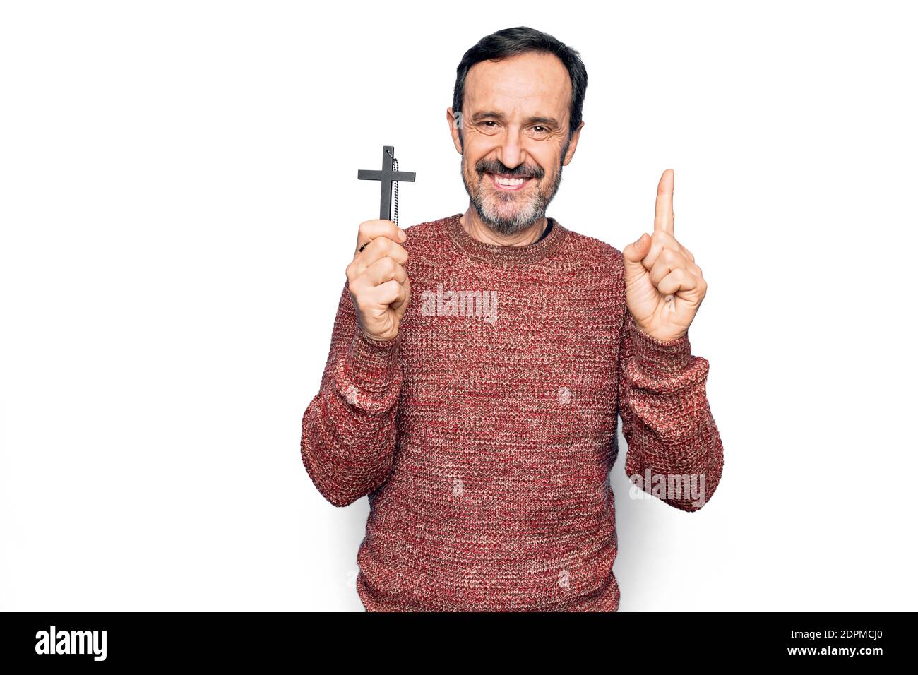 Middle age handsome catholic man praying holding christian cross over ...
