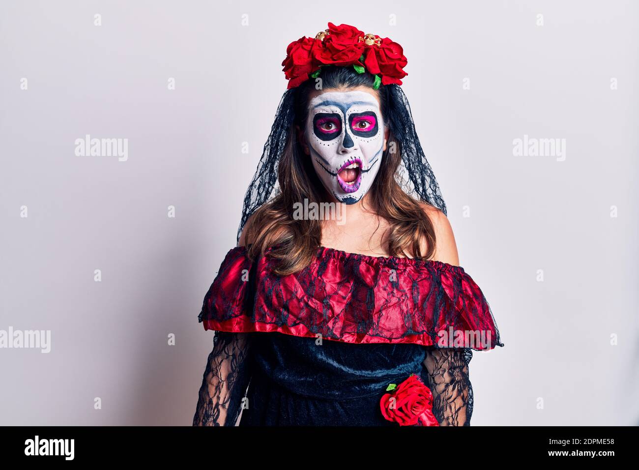 Young woman wearing day of the dead costume over white in shock face ...
