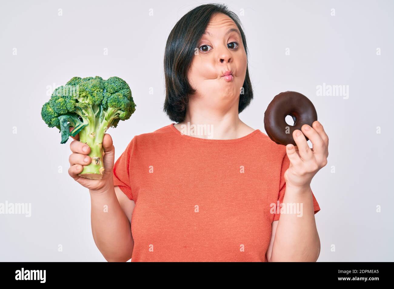 Brunette woman with down syndrome holding broccoli and chocolate donut ...