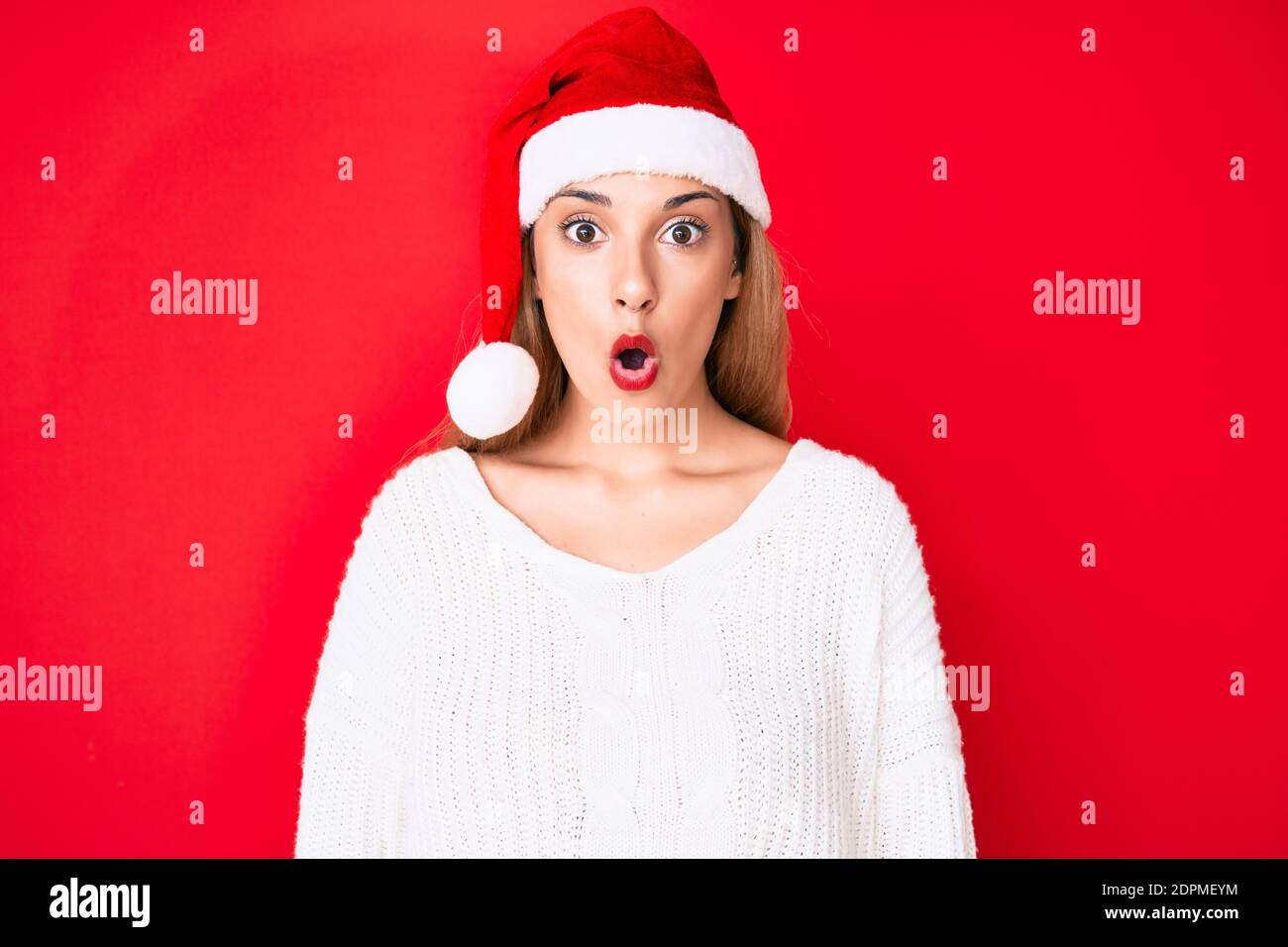 Young brunette woman wearing christmas hat scared and amazed with open ...