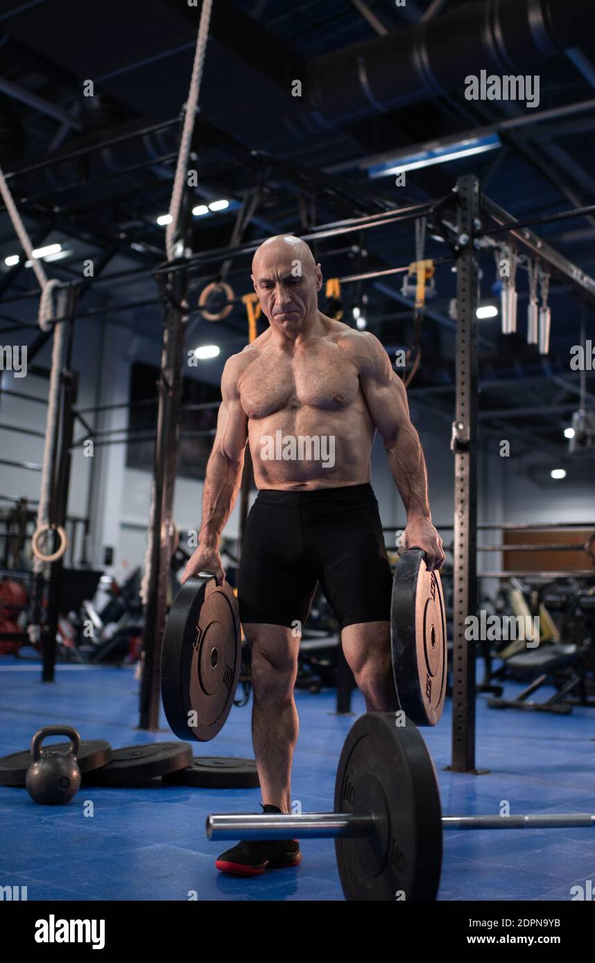 Full body muscular shirtless senior man carrying heavy weight plates ...