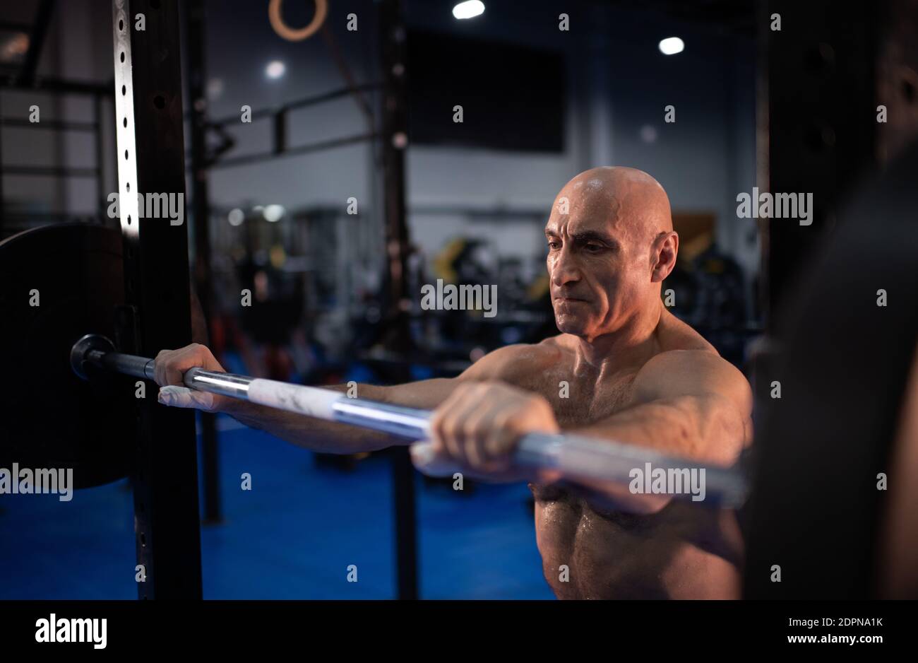Muscular elderly sportsman taking heavy barbell from rack before ...