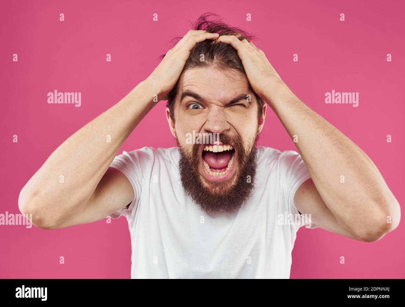 An angry man touches his head with his hands on a pink background Copy ...