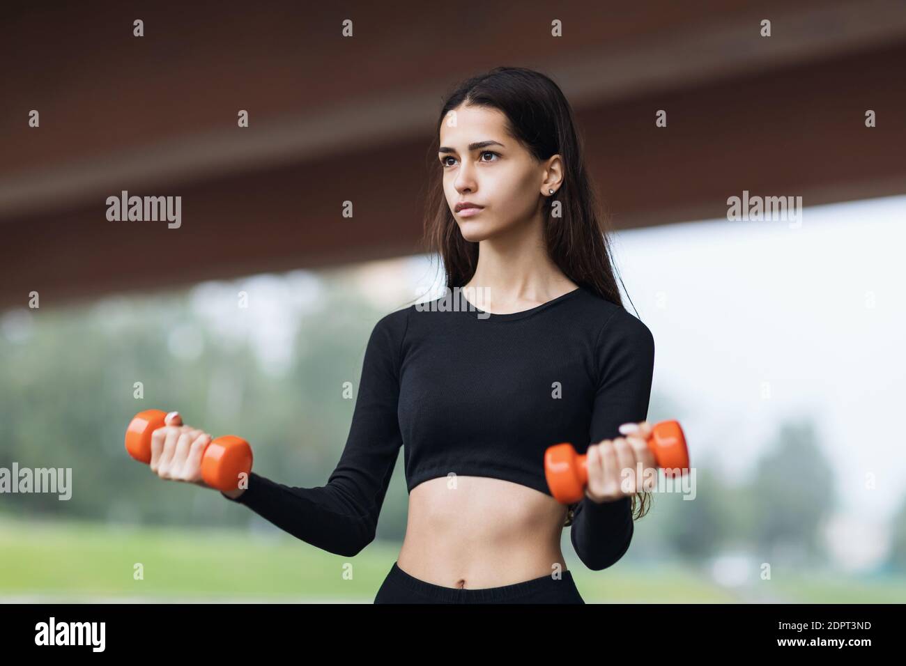 Beautiful young woman performs exercises with dumbbells in the street ...