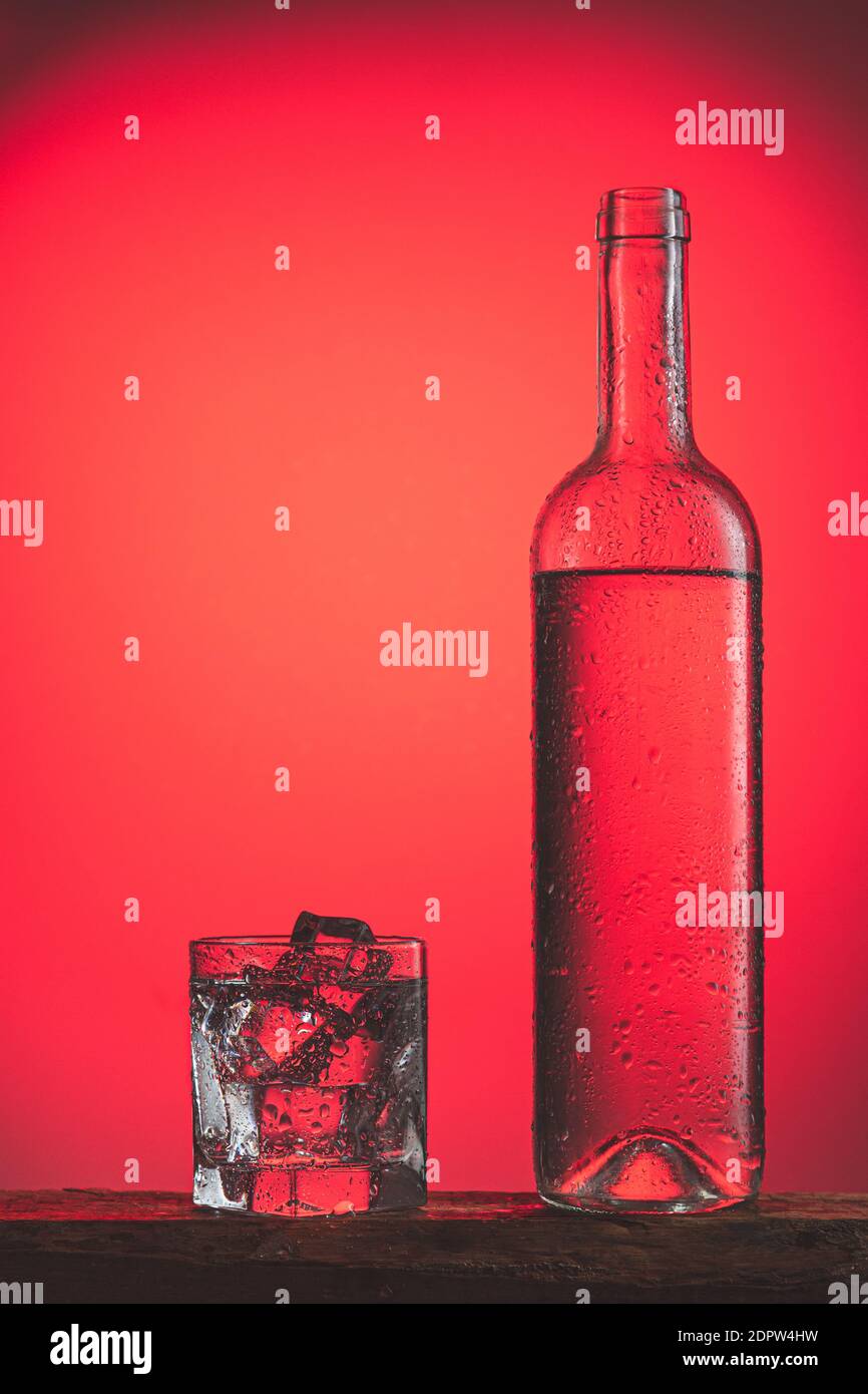 Refreshing cold drink in bottle with drops, and glass with ice on red ...