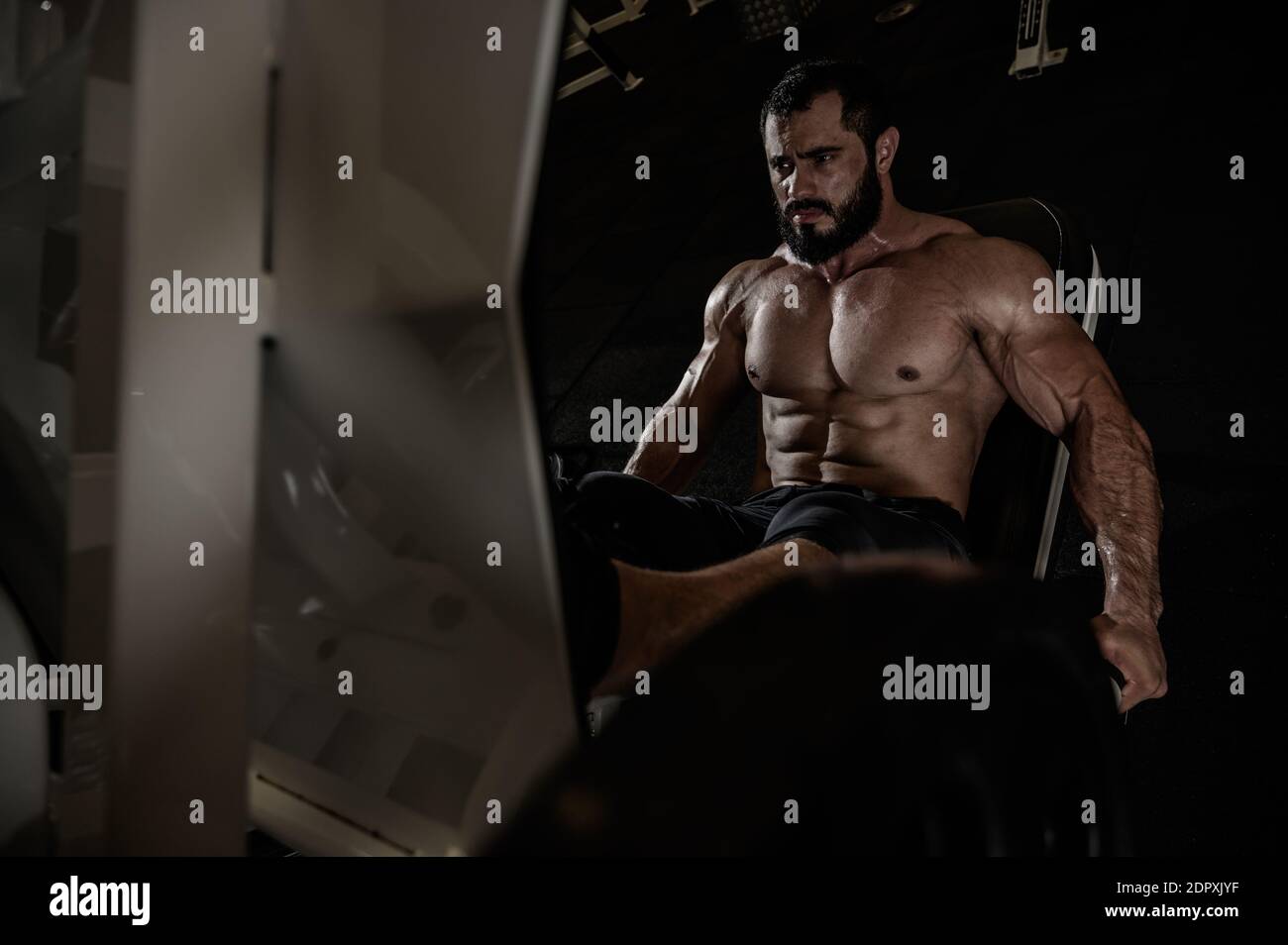 strong young bearded man workout training in leg press machine in dark ...
