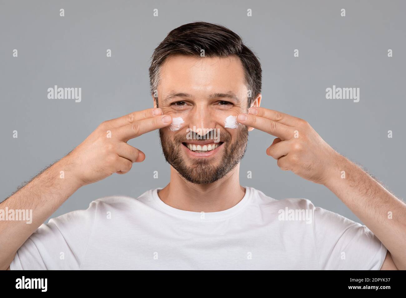 Smiling handsome man applying cream on his face, grey background Stock ...