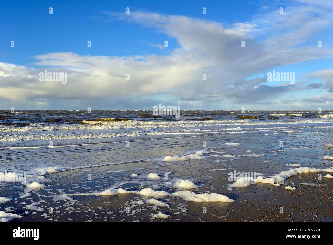 Waves on a sandy beach with foam formation, blue sky with deep swelling ...