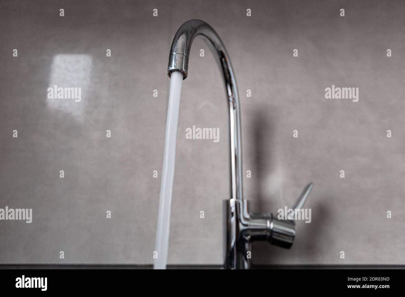 Horizontal view of the silver faucet in the bathroom. Water is flowing ...