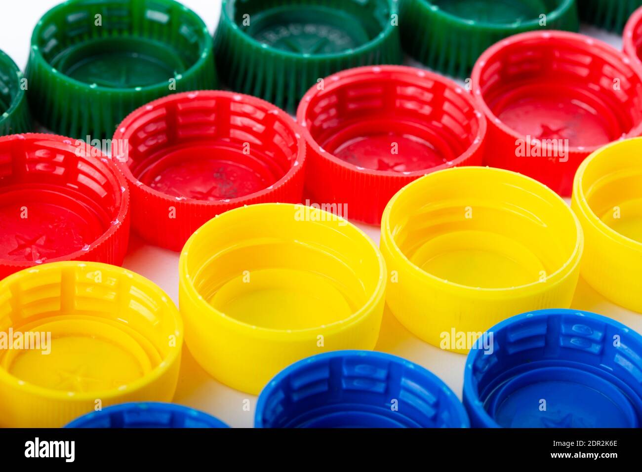Plastic multi-colored bottle caps are arranged in rows on a white ...